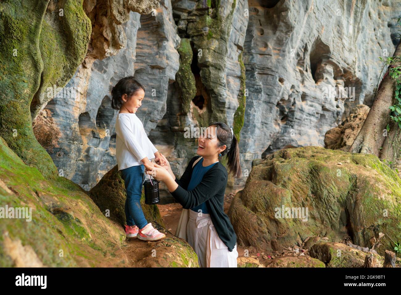 Southeast Asian mother with her daughter playing on a mossy rocky cave ...