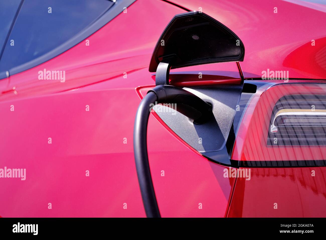 Beautiful red Tesla EV car in charging station with the power cord ...