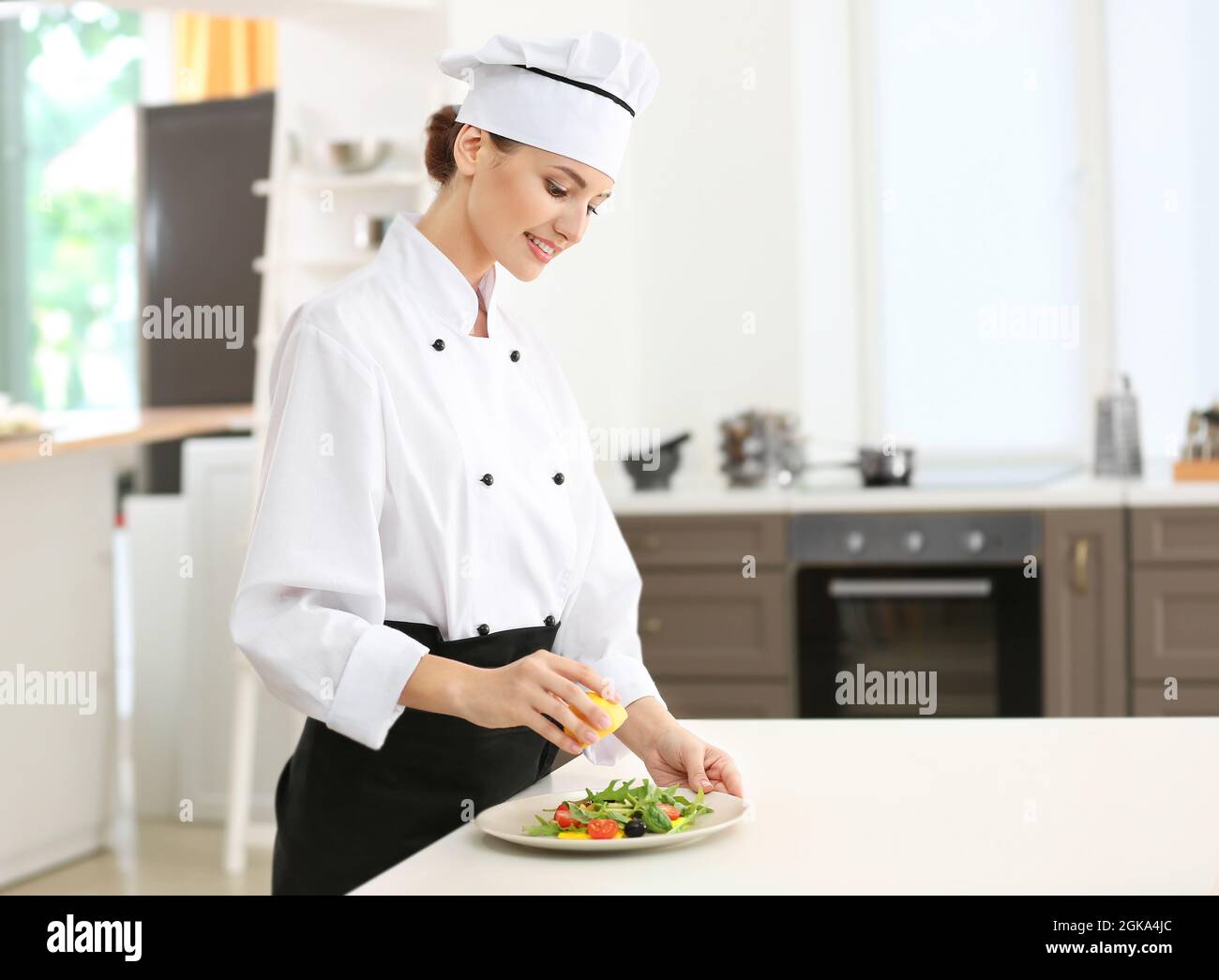 Young female chef dressing salad with lemon juice in kitchen Stock ...