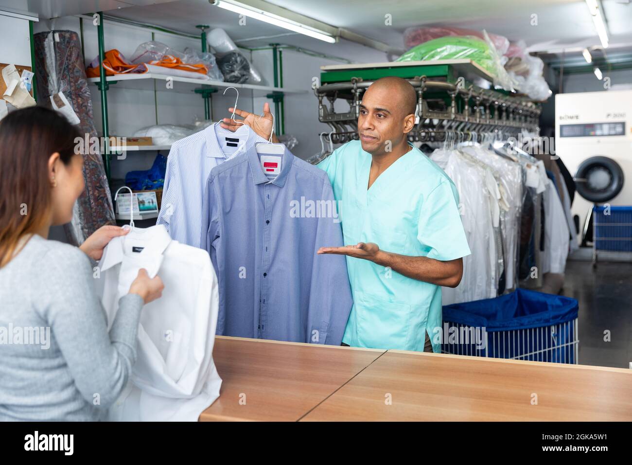 Laundry employee handing out clean clothes to client Stock Photo - Alamy