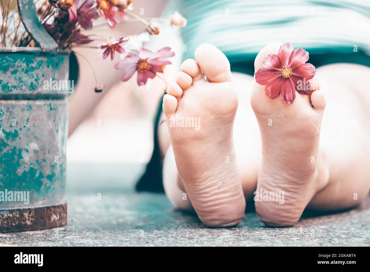 Child with cosmos flowers between toes lying near a vintage watering ...