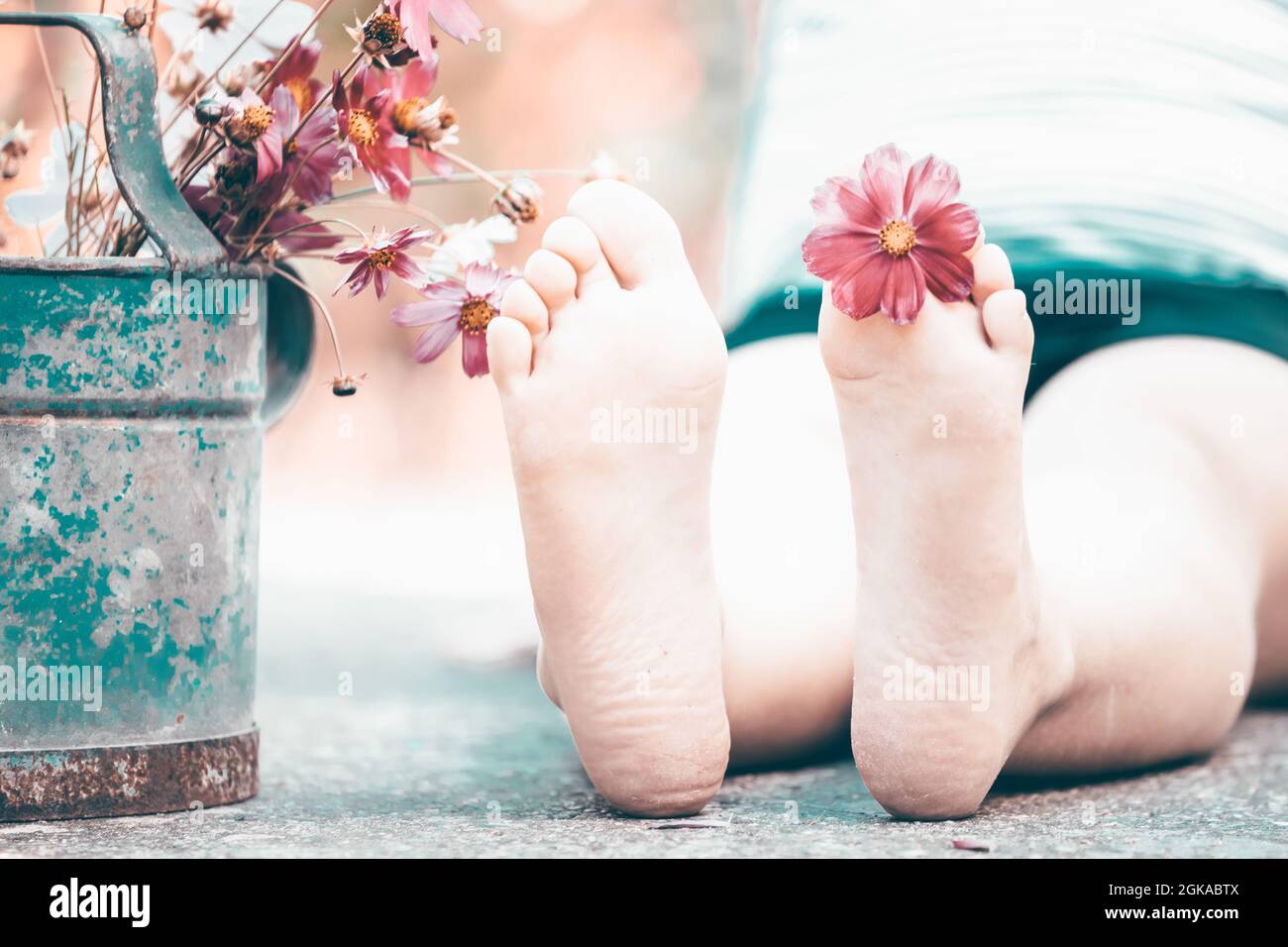 Child with cosmos flowers between toes lying near a vintage watering ...