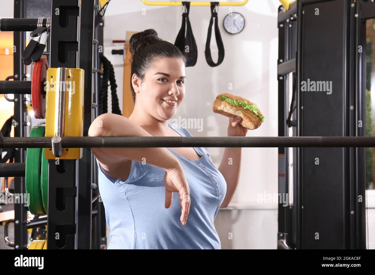 Overweight young woman eating sandwich in gym Stock Photo - Alamy