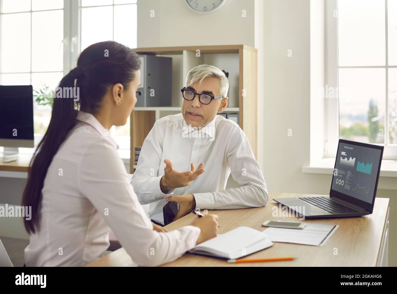 Two business people sitting at office desk with laptop and discussing ...