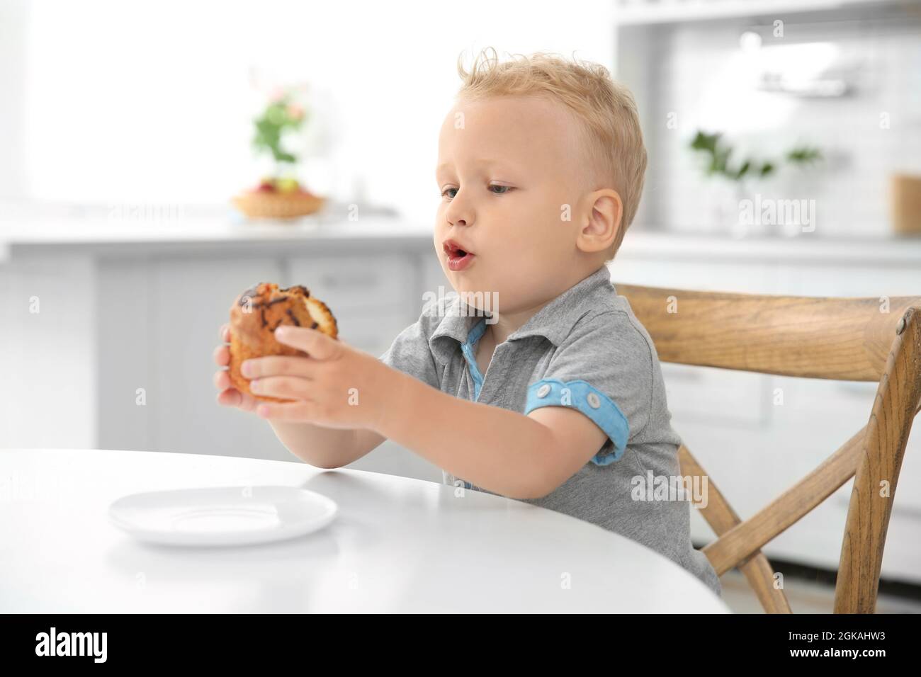 Adorable little boy holding big muffin with both hands in kitchen Stock ...