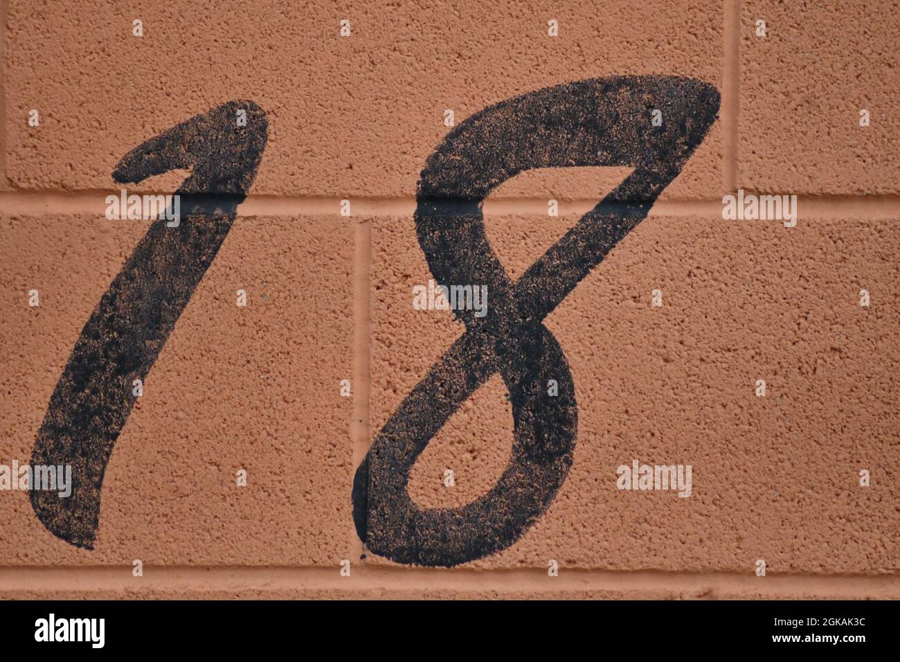 A black number 18, eighteen painted in black on an orange breeze block ...