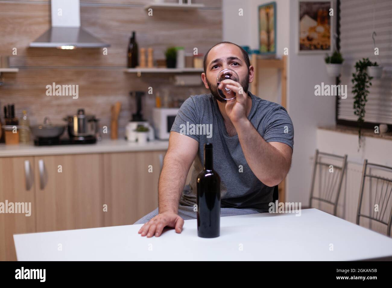 Pensive man drinking glass of wine while sitting alone and depressed ...