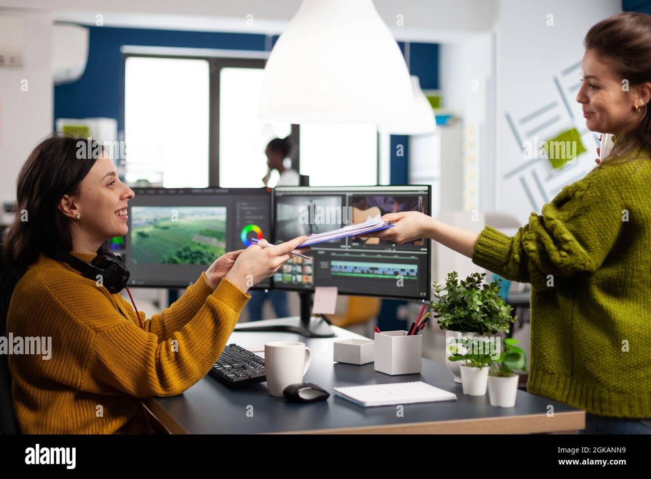 Creators drinking coffee and talking during office break sitting at desk in digital agency ...