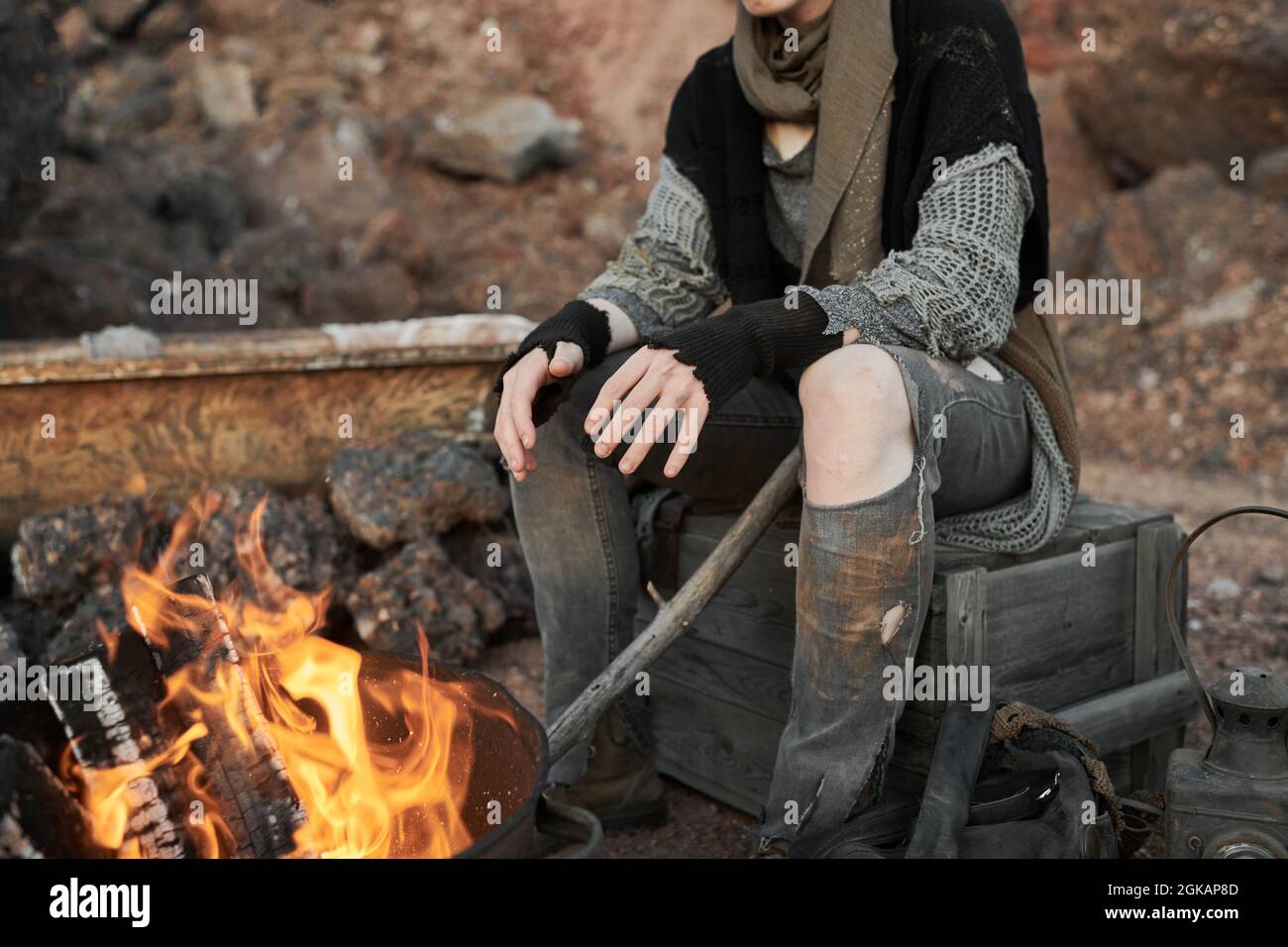 Close-up of homeless woman in torn clothes warming up near the fire ...