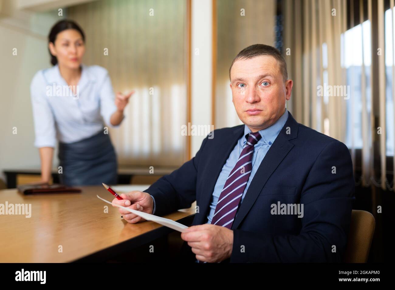 Upset businessman sitting with papers in office with disgruntled female ...