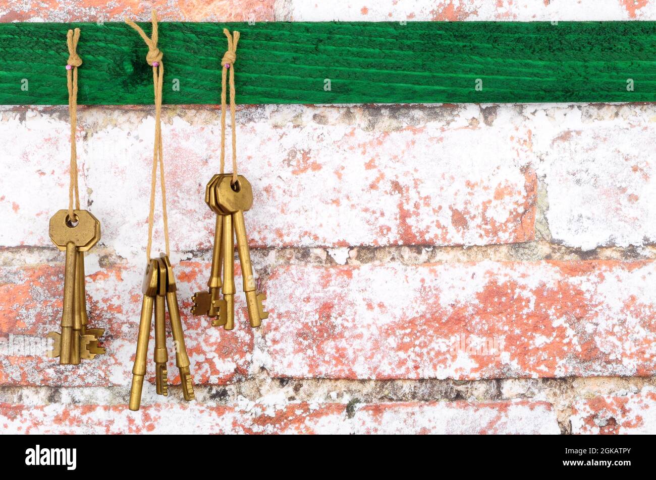 Old brass metal door keys hanging from string against a rustic brick ...