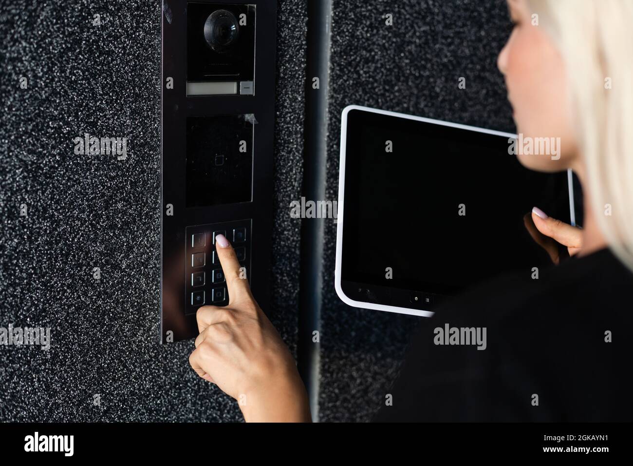 Happy woman ringing on doorbell at building entrance. Using intercom ...