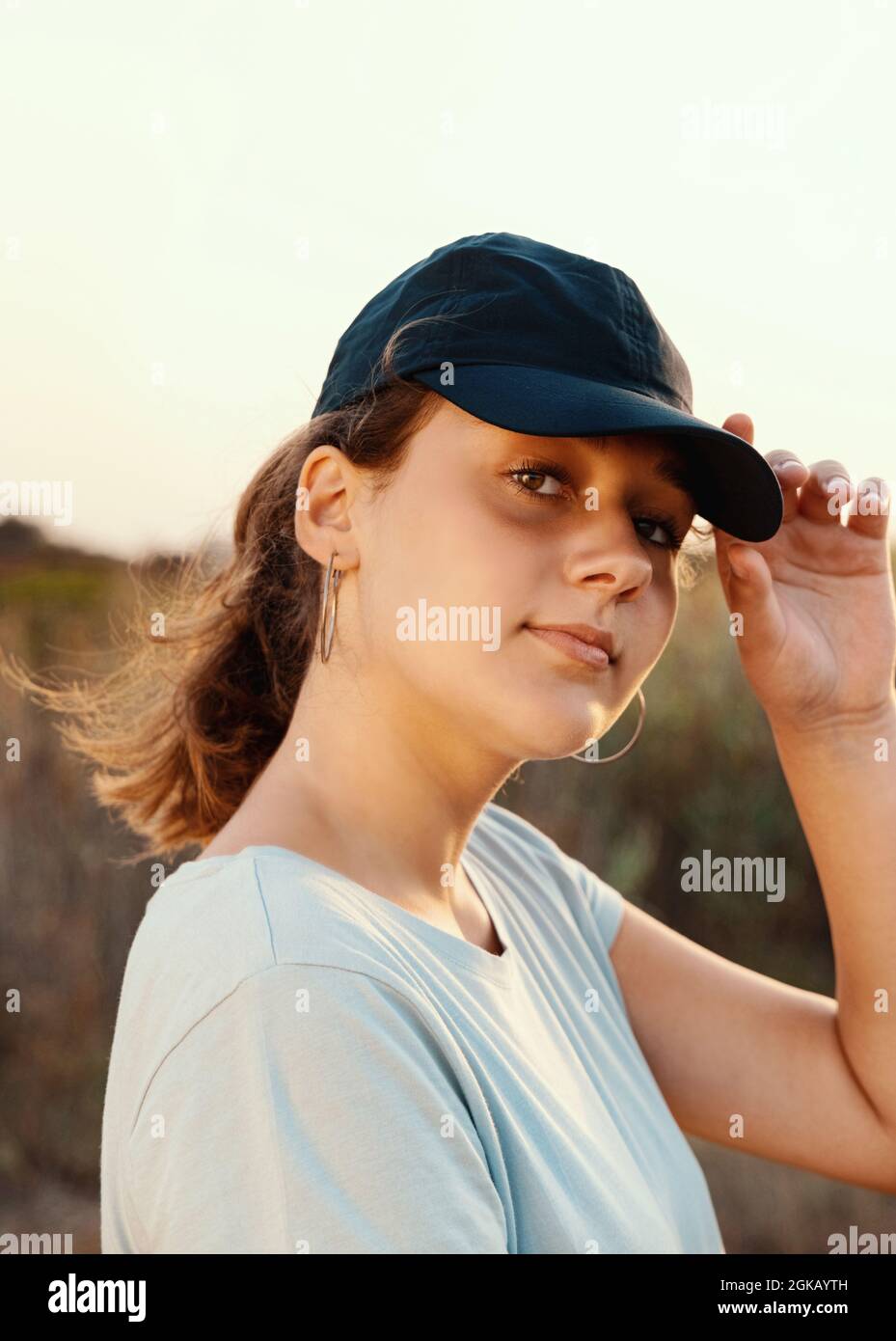 Teenager standing by the field at sunset and looking stright at camera ...