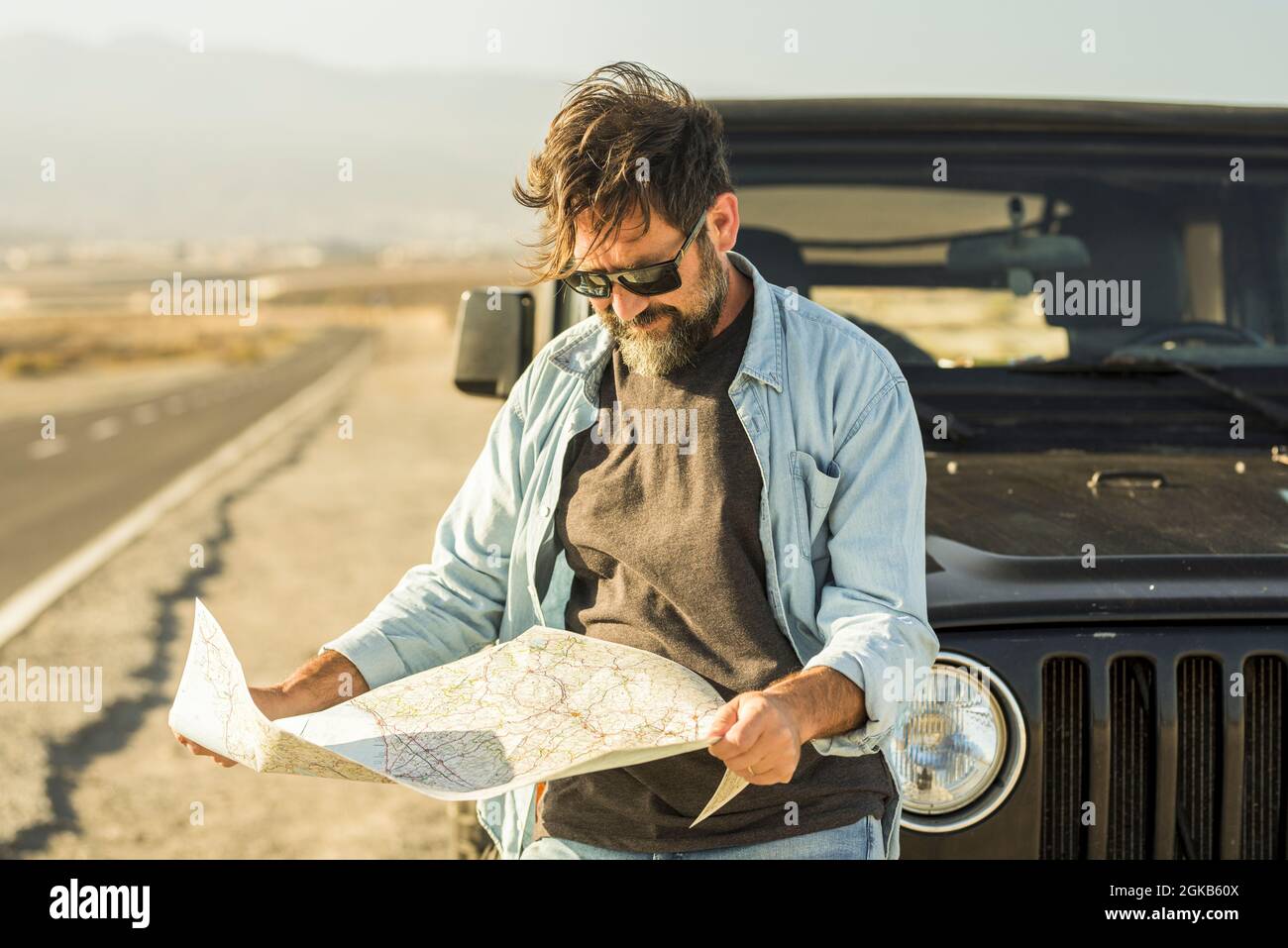 Man looking at map leaning on vehicle at roadside. Mature man checking ...