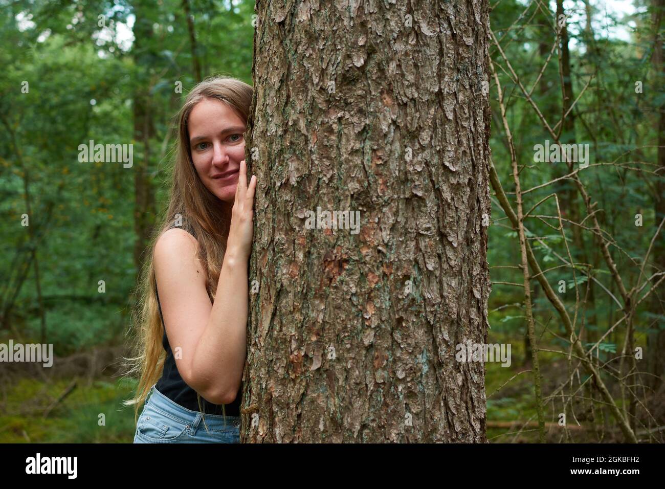 Beautiful blonde girl looking behind the tree with a smile on her face ...