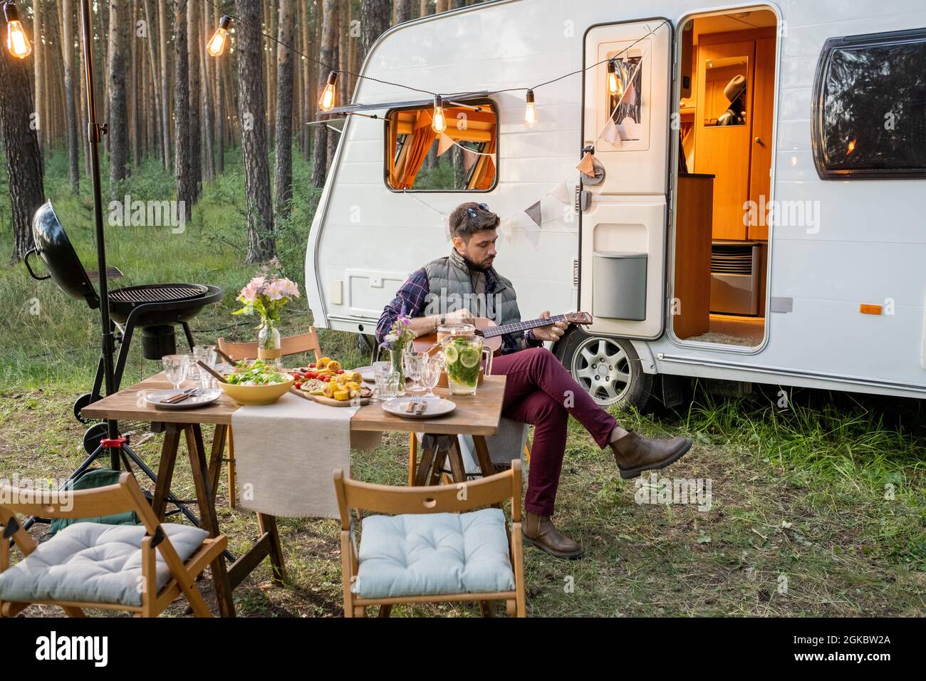 Restful guy playing guitar by served table against house on wheels in ...