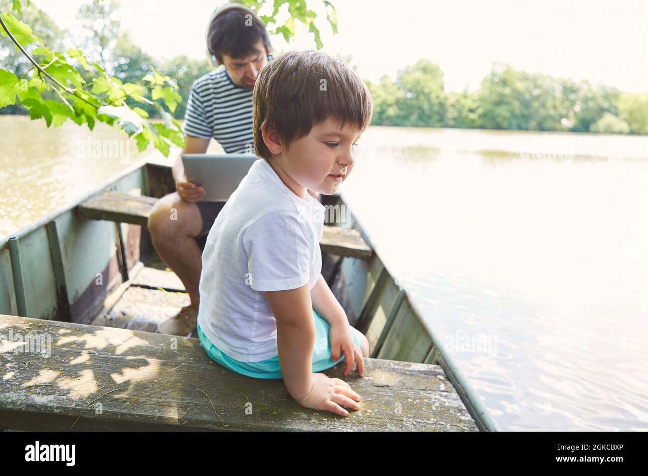 Boy in boat on a lake on summer vacation with father on laptop in ...