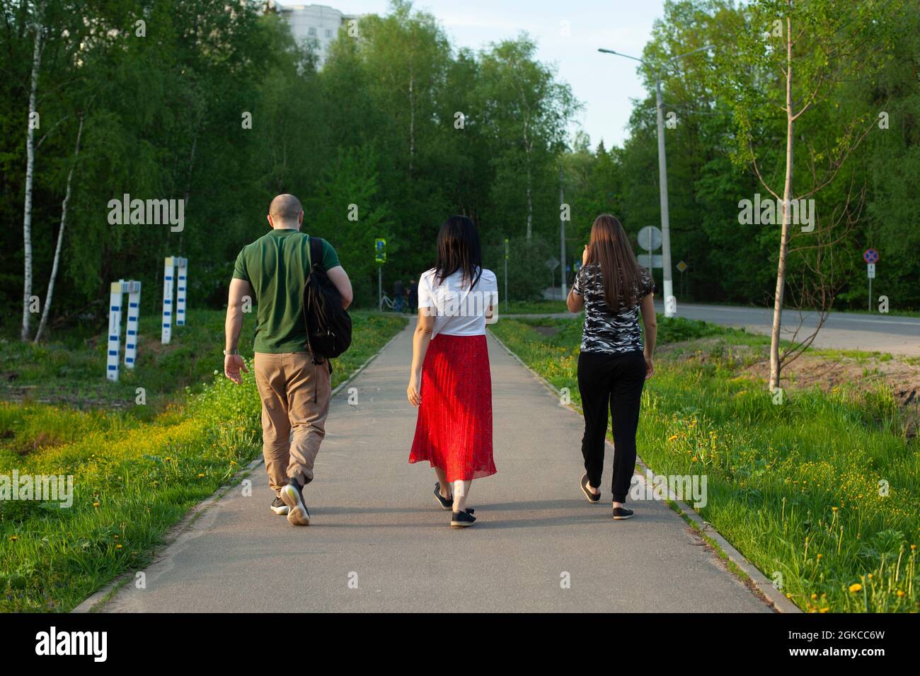 A guy and two girls are walking along the road. Young people are ...