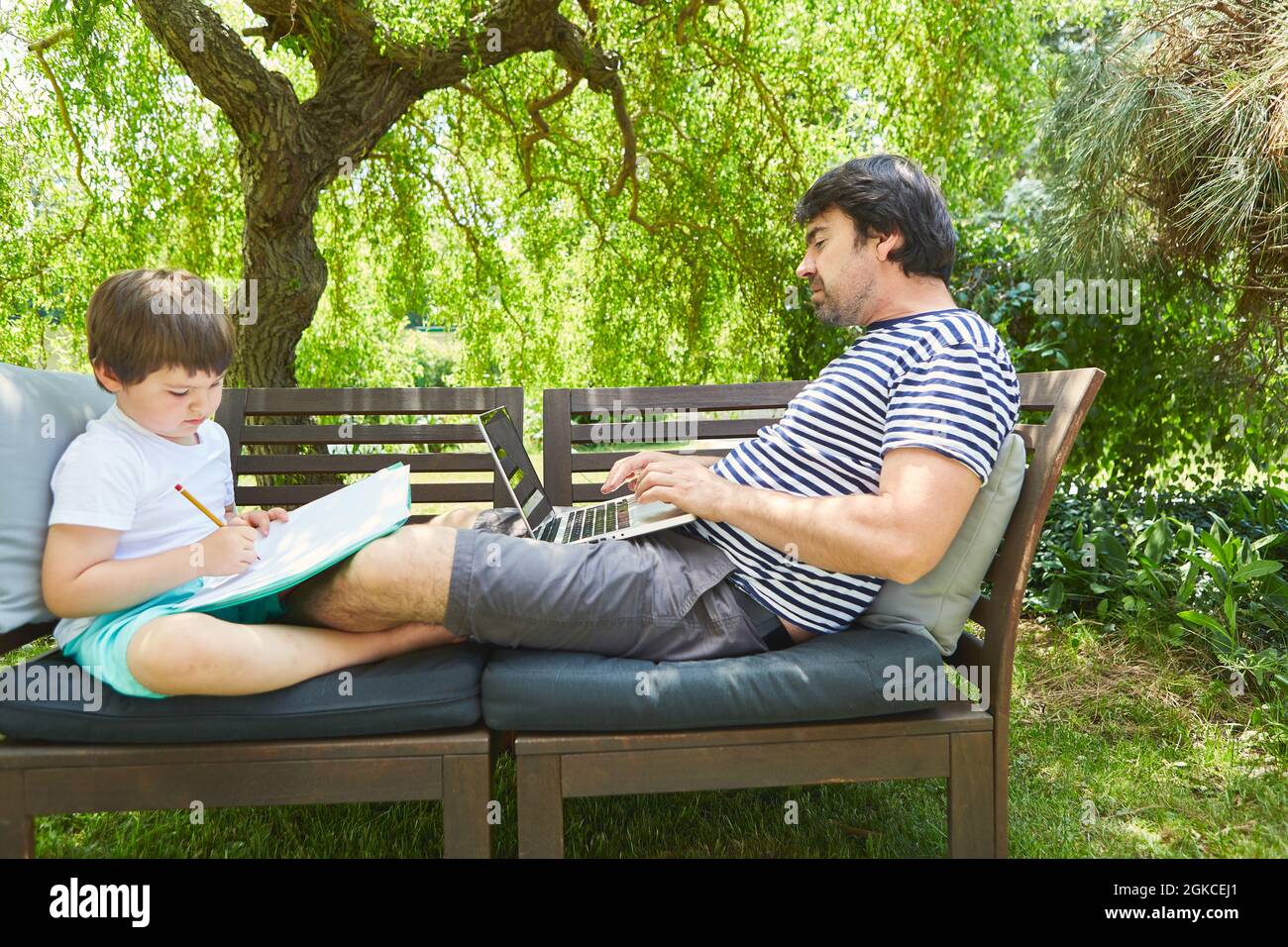 Single father on laptop PC in green garden in summer with his son Stock ...