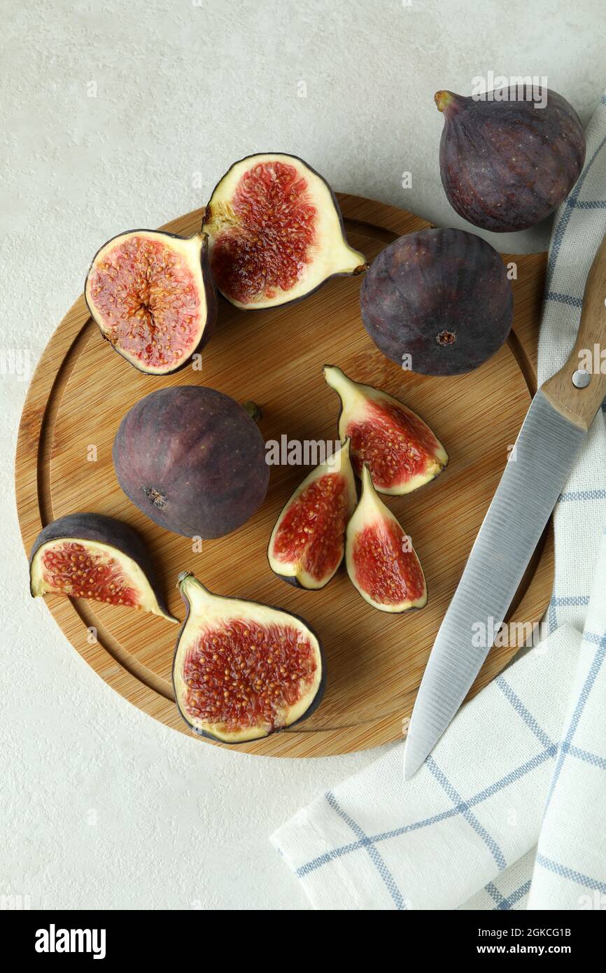 Board with fig, knife and kitchen towel on white textured table Stock ...