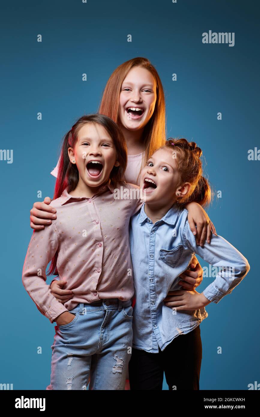 three kids girls standing together on blue background Stock Photo - Alamy
