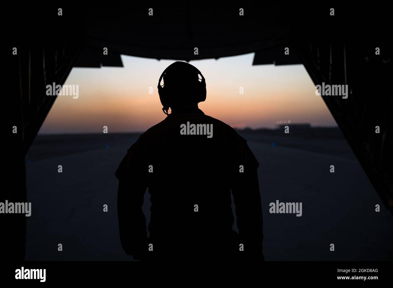 A U.S. Air Force loadmaster watches as the sun sets from the back of a ...