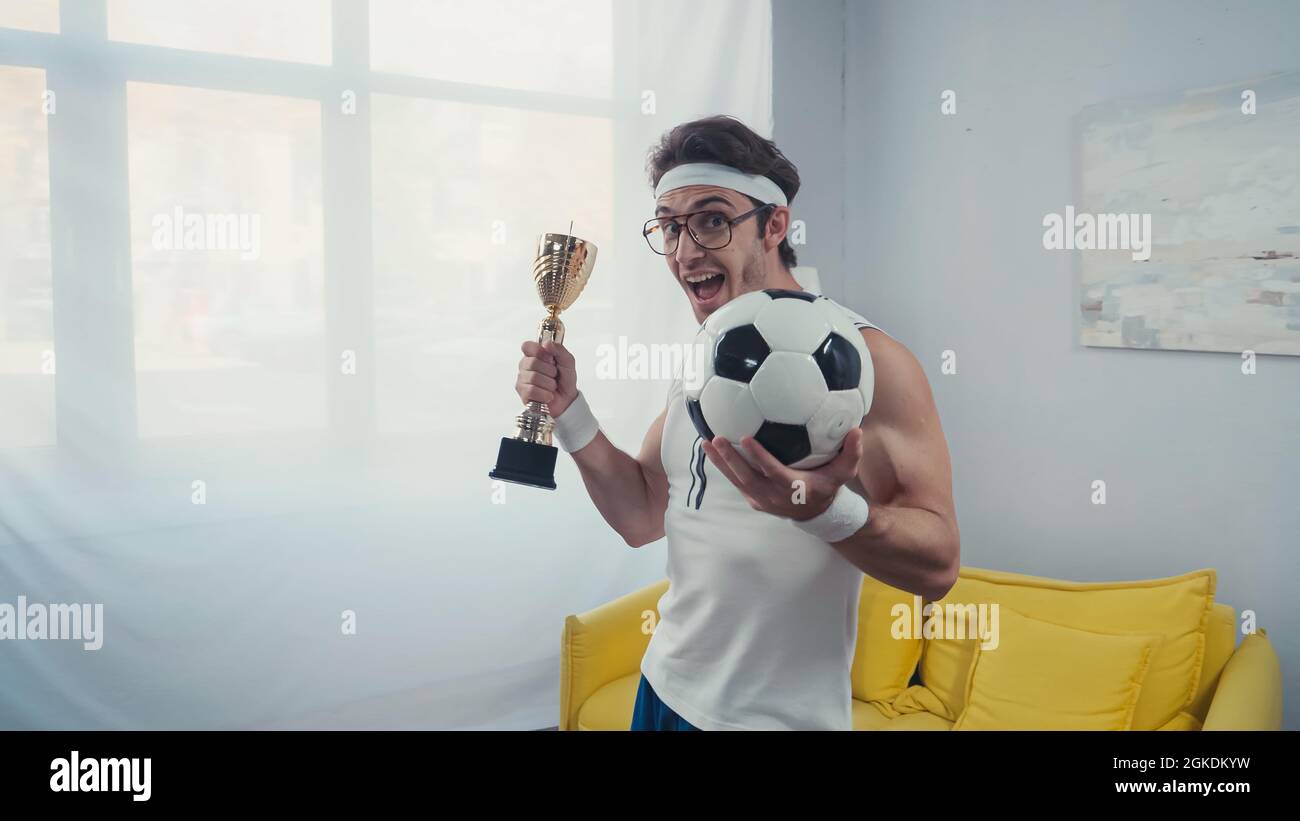 Excited football player with trophy cup and soccer ball celebrating win ...