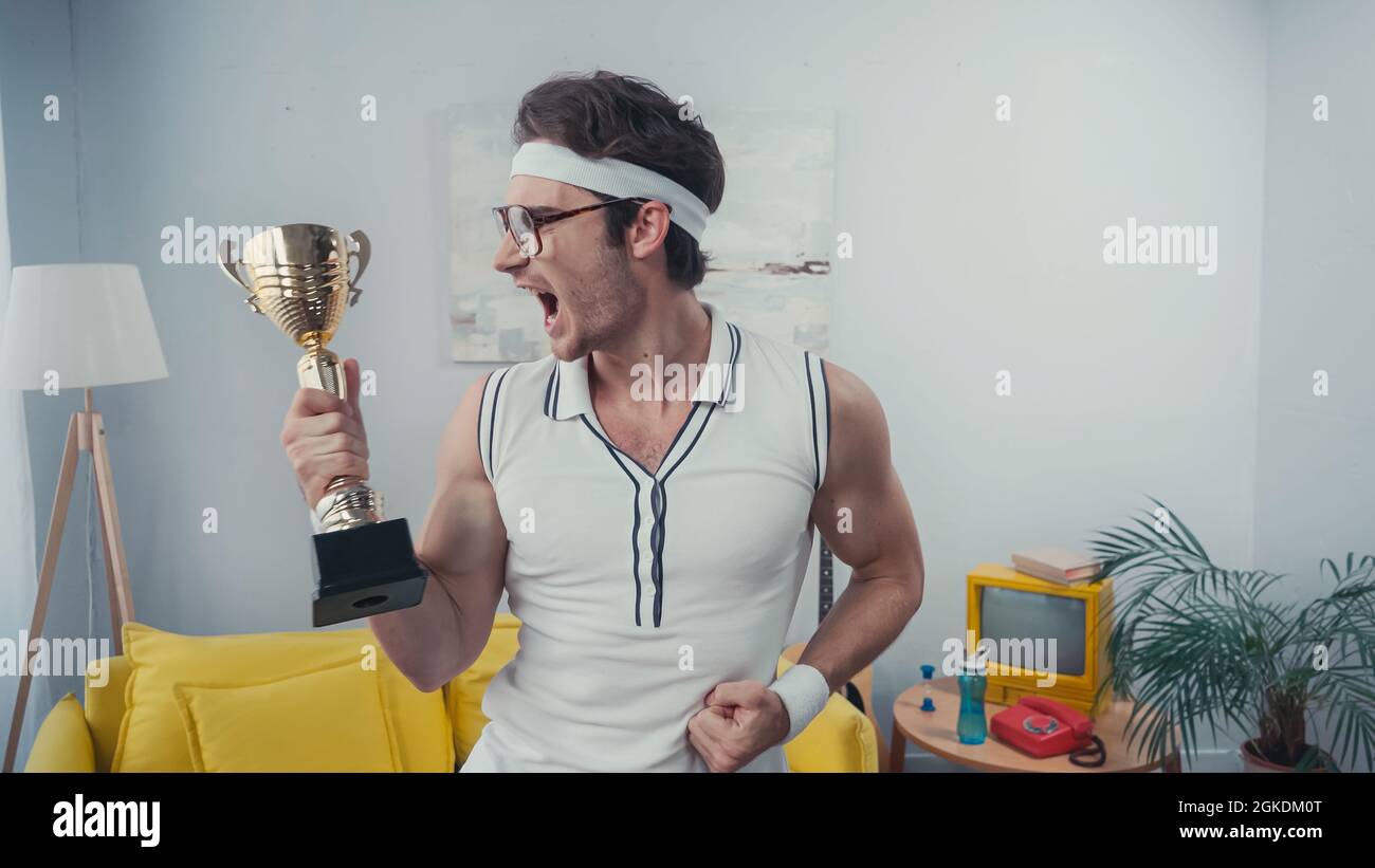 excited sportsman in eyeglasses screaming while holding golden trophy ...