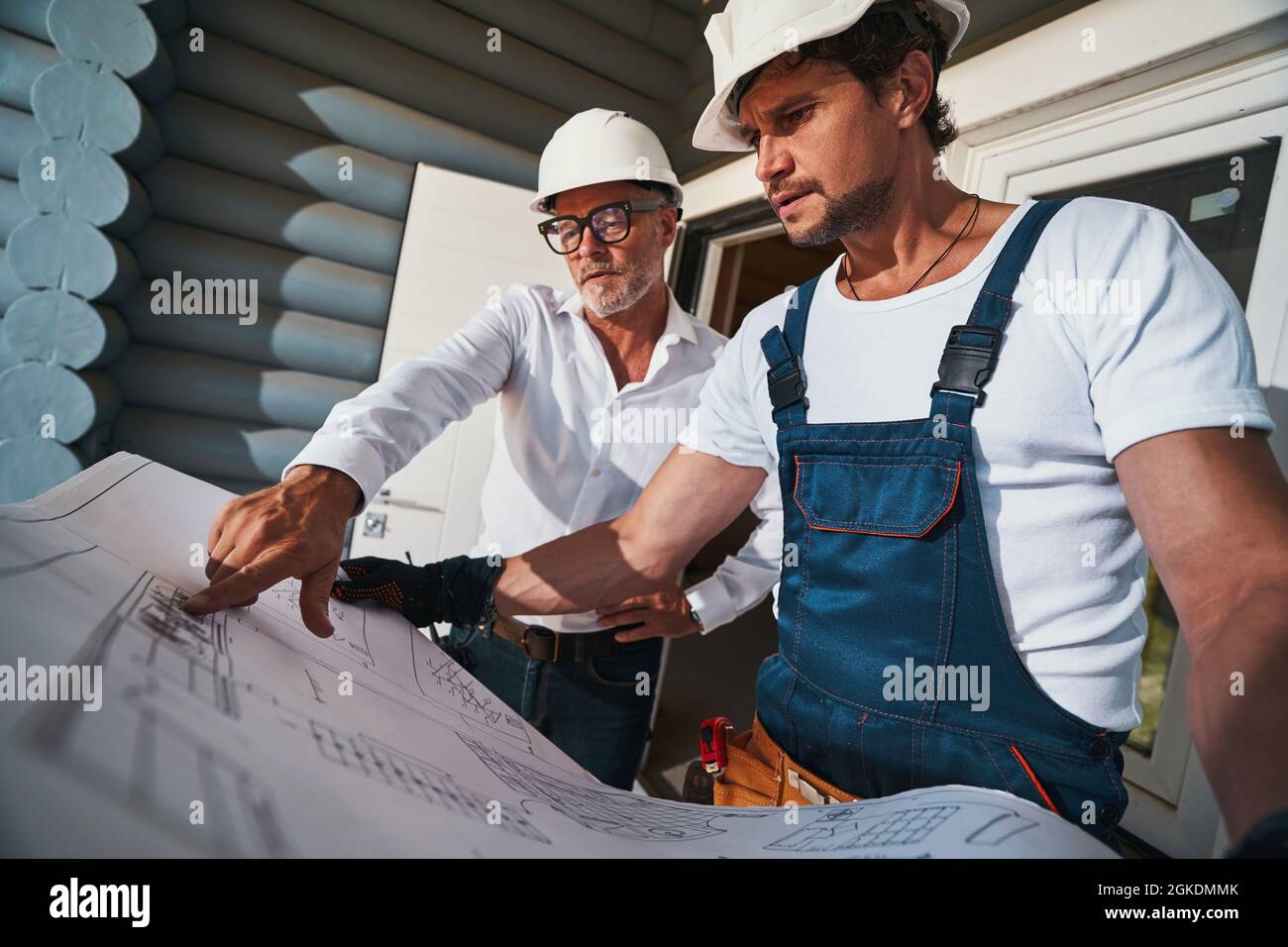 Civil engineer showing place in blueprint to worker Stock Photo - Alamy