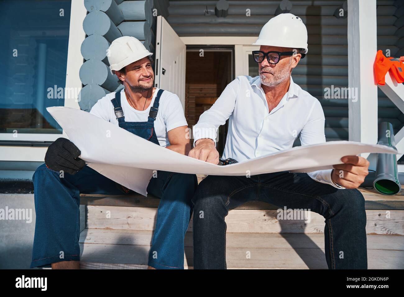 Builders sitting on porch stairs and discussing construction plans ...