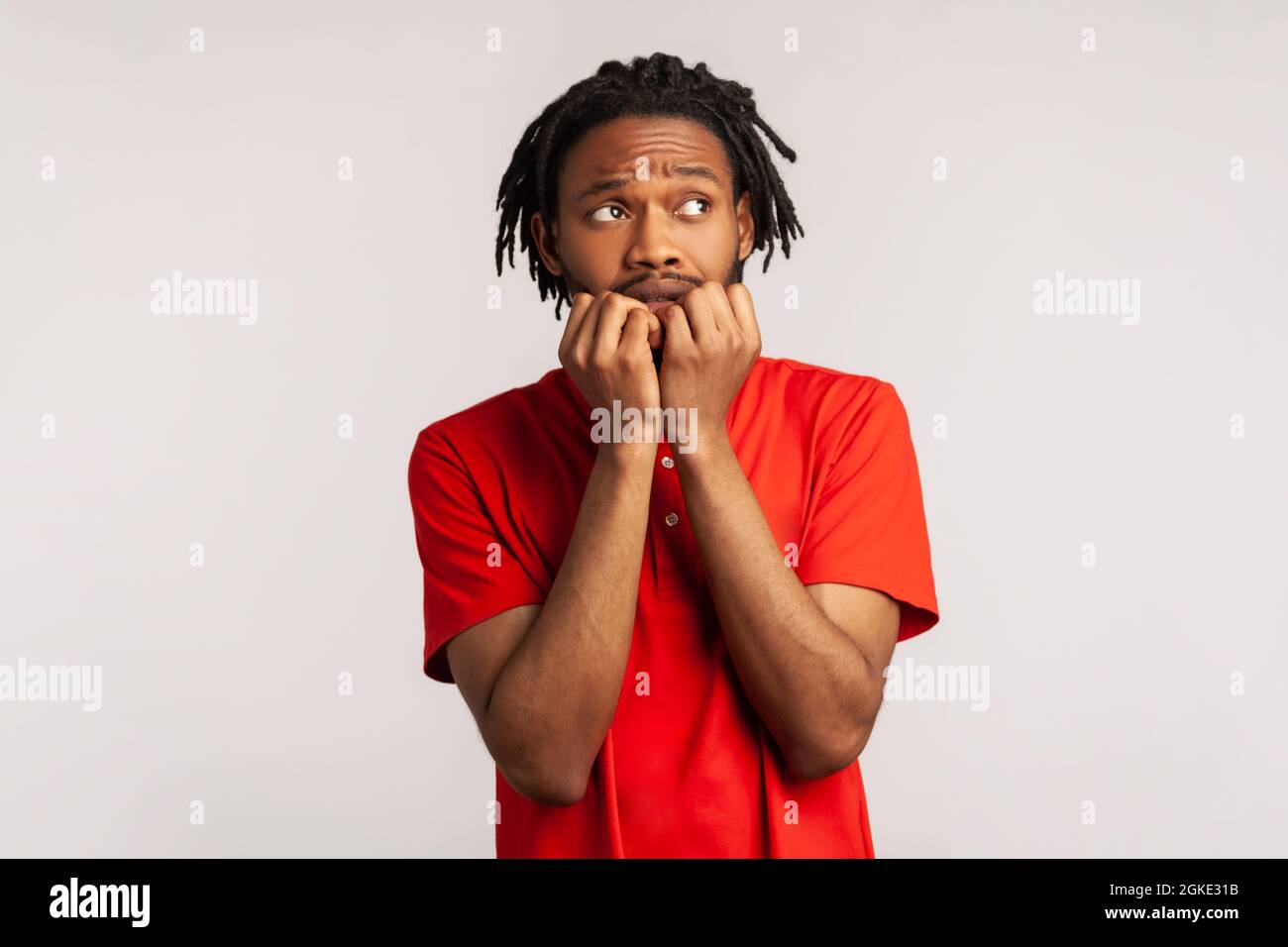 Anxious man with dreadlocks wearing red casual style T-shirt, biting ...