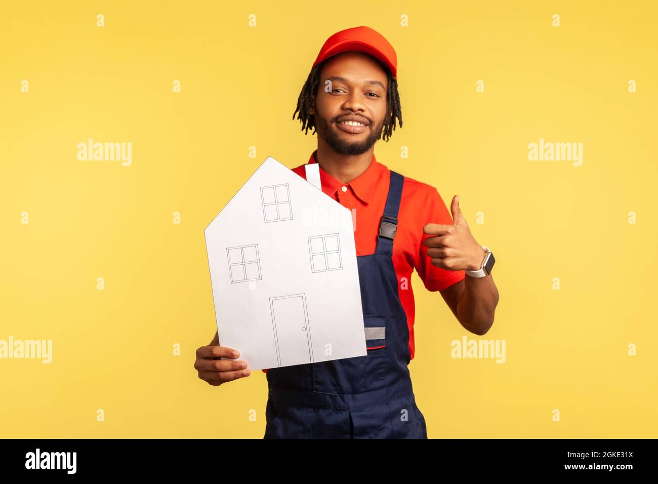 Positive handyman, building worker in blue overalls holding paper house ...