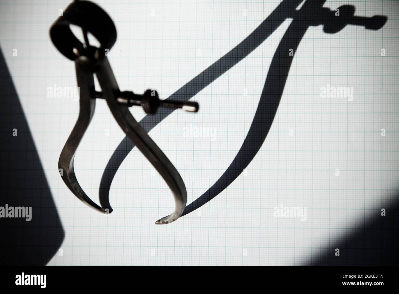 Metal outside spring calipers casting abstract shadow on piece of graph ...