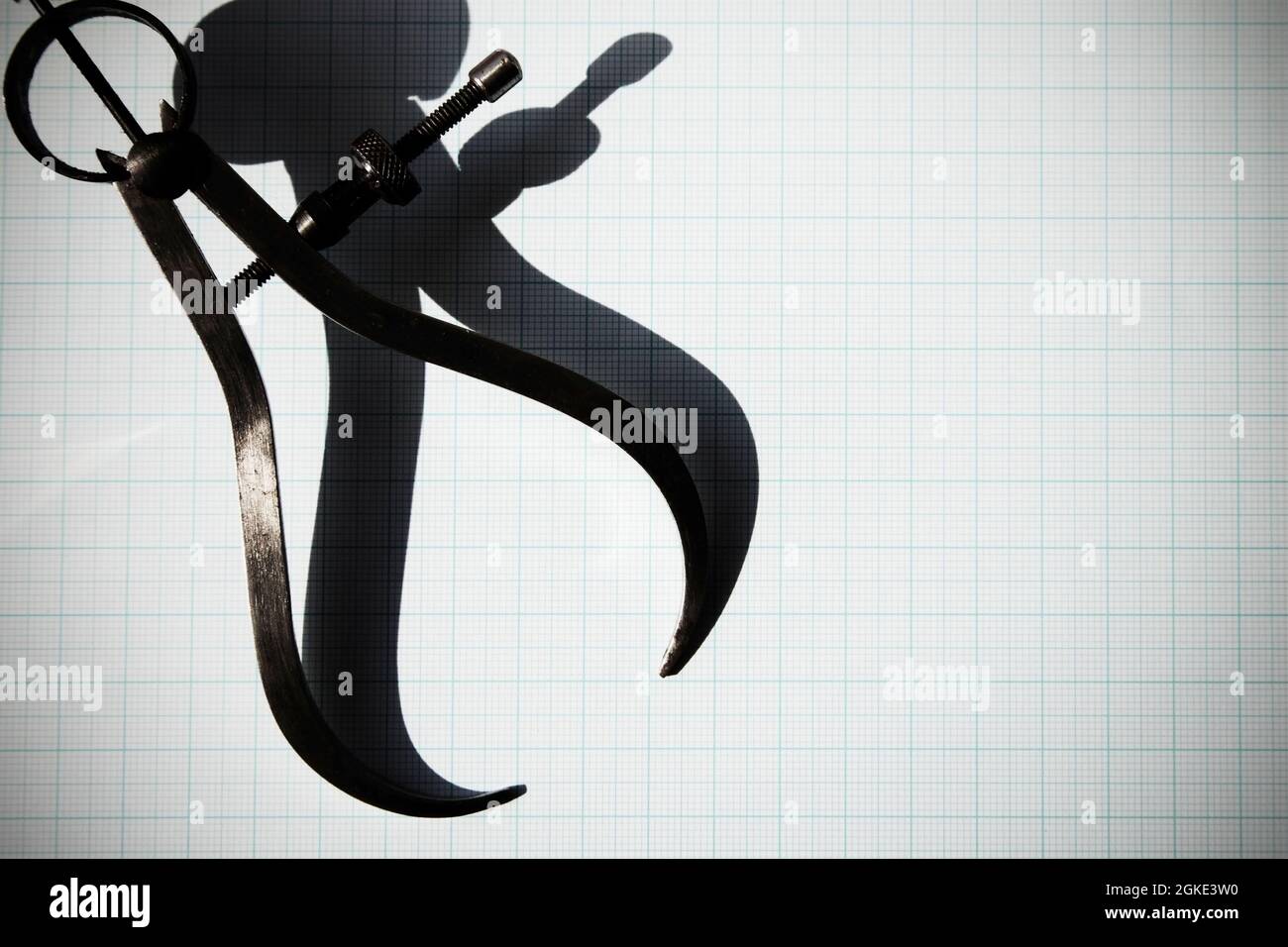 Metal outside spring calipers casting abstract shadow on piece of graph ...
