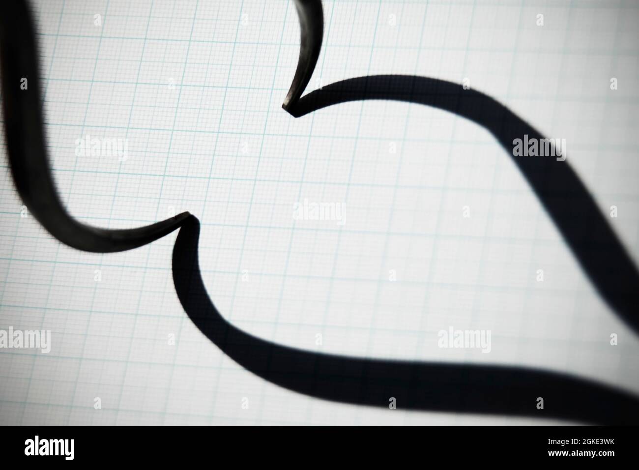 Metal outside spring calipers casting abstract shadow on piece of graph ...