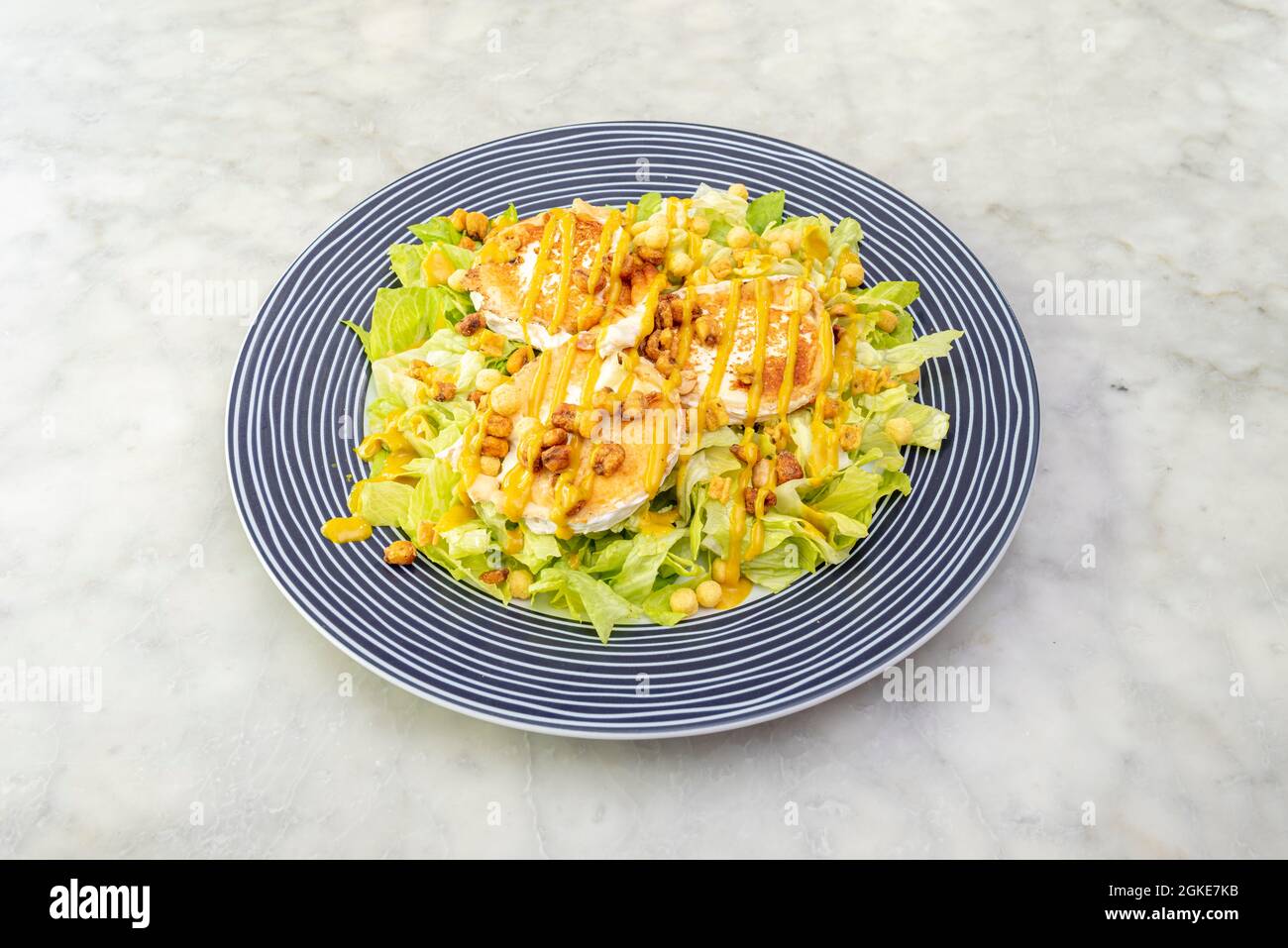 Goat cheese salad with lettuce and nuts in nice white striped plate on ...