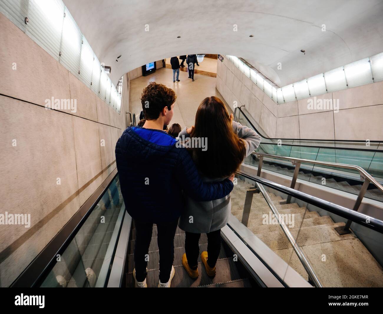 Rear view of young couple descending on escalator to change the train ...