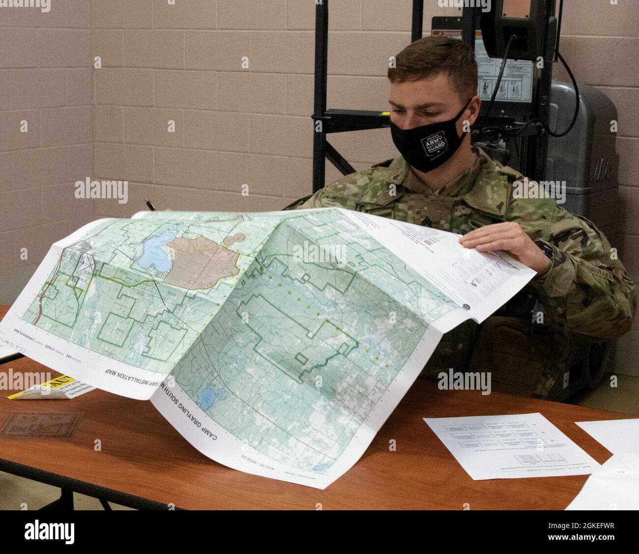 A Michigan Army National Guard soldier opens a map to plot his ...
