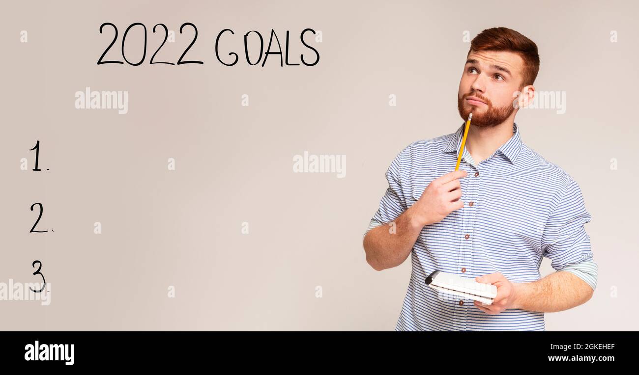 Thoughtful young man making 2022 goals list, dreaming, making new year ...