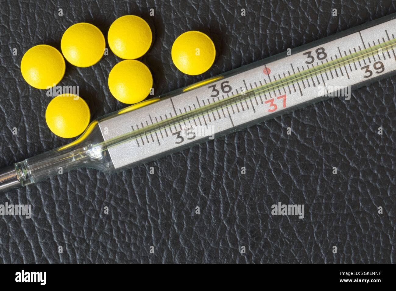 thermometer for measuring fever with yellow pills on a black background ...