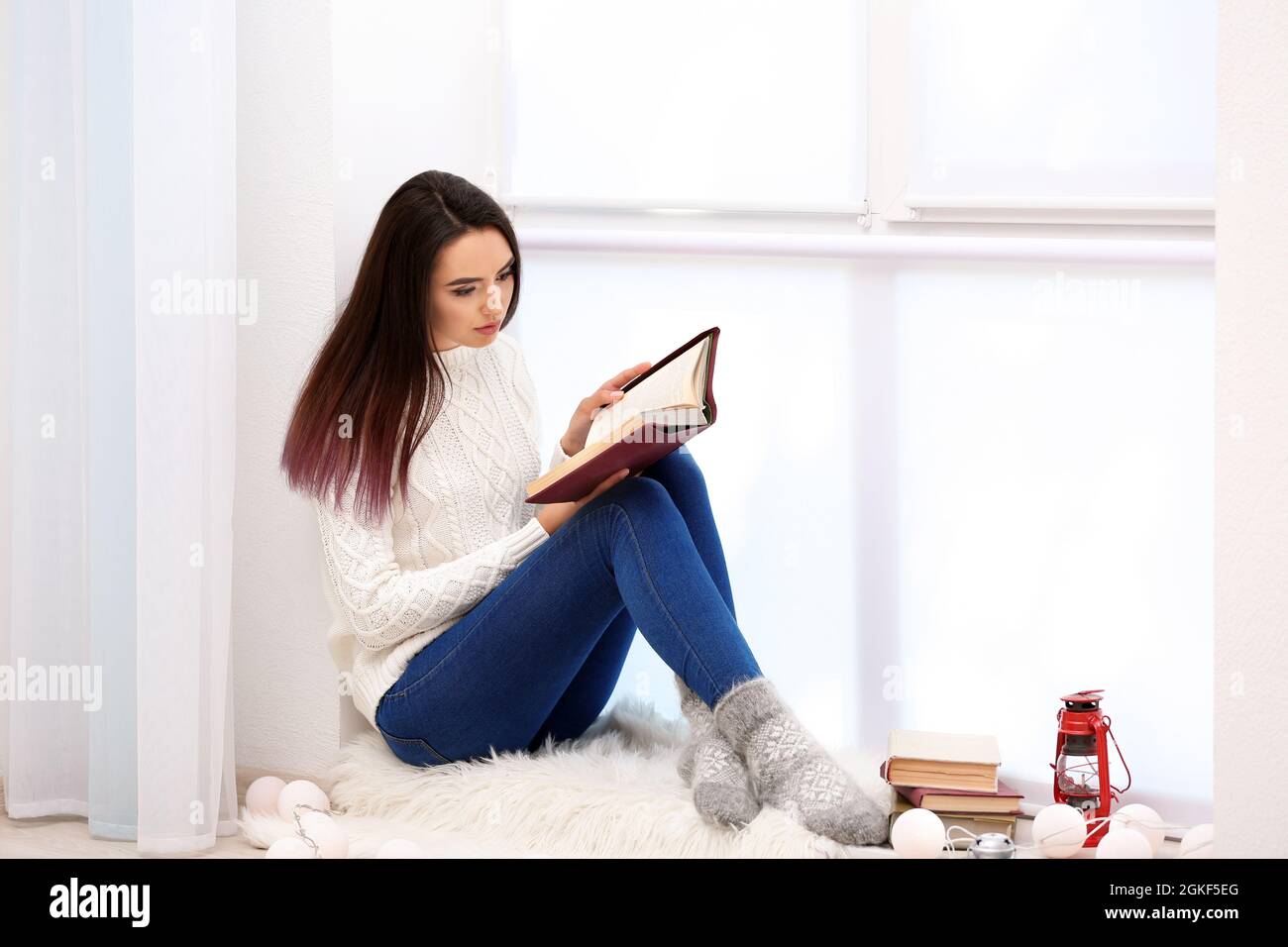Attractive young lady reading book on window sill at home Stock Photo ...