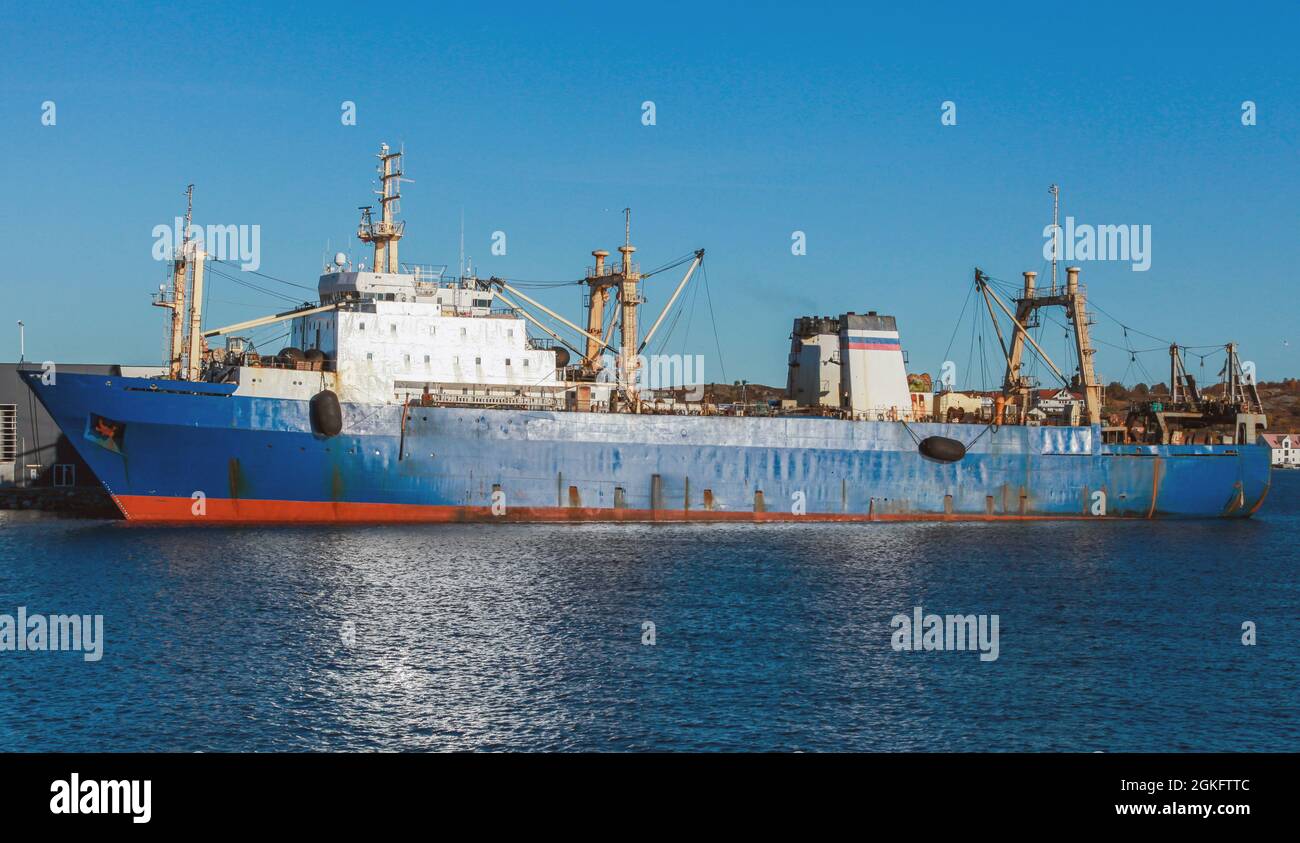 Trawler ship with blue hull is moored in Norwegian port on a sunny day ...