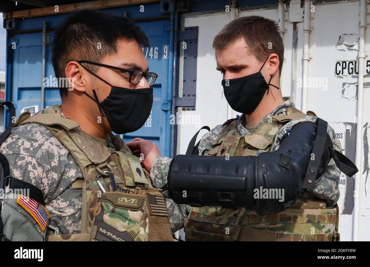 Spc. Tristan Parker straps a protective shoulder pad on to Spc. David ...