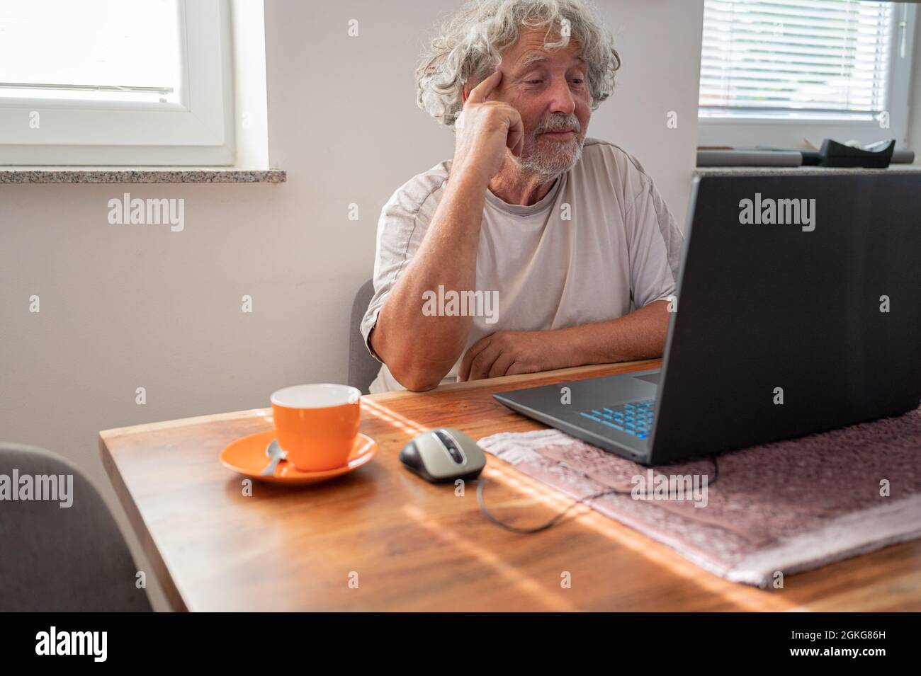 Senior man, grandpa, with grey curly hair sitting at dining table ...
