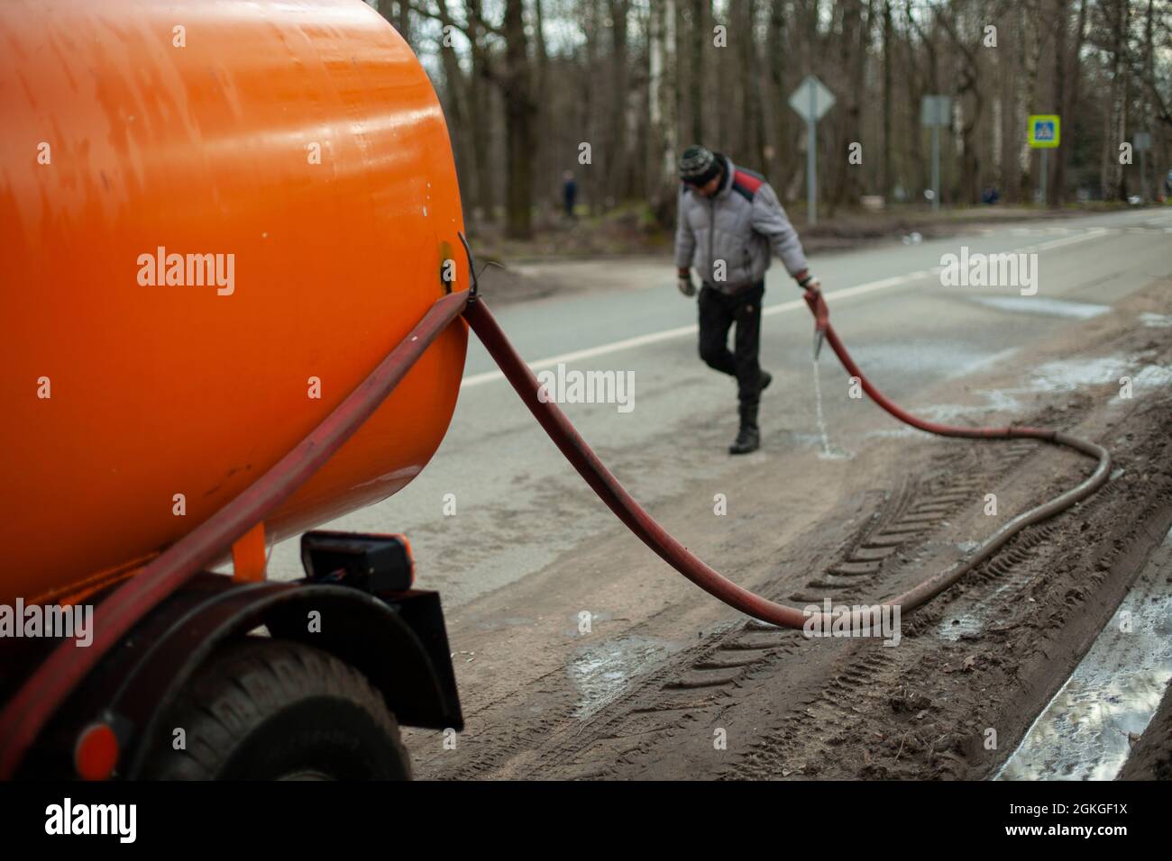Barrel of water. Washing the side of the road. A man with a hose goes ...
