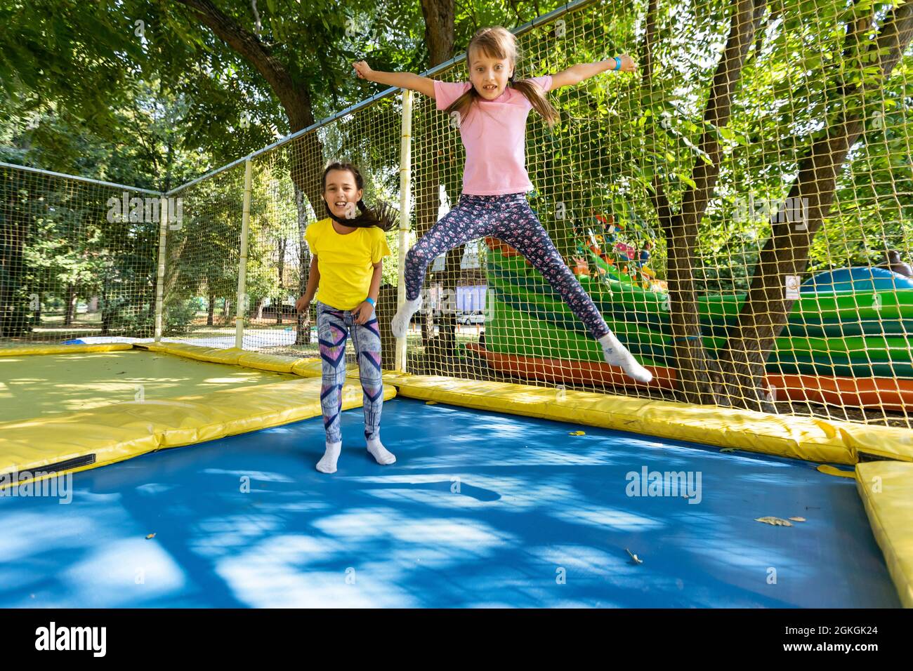 Two little girls in the summer jump on a trampoline, smiling and ...