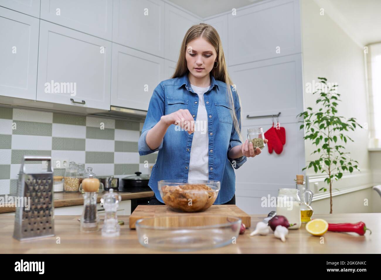 Young woman cooking chicken, marinating with spices black pepper salt ...