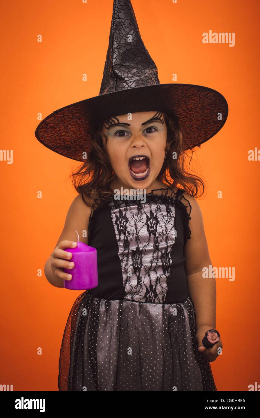 Vertical shot of a kid wearing a witch costume with a candle in her ...
