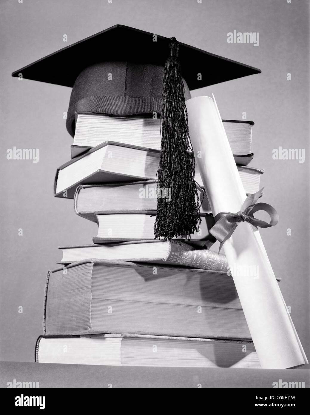 1970s STACK OF BOOKS WITH DIPLOMA LEANING ON SIDE AND MORTARBOARD ...