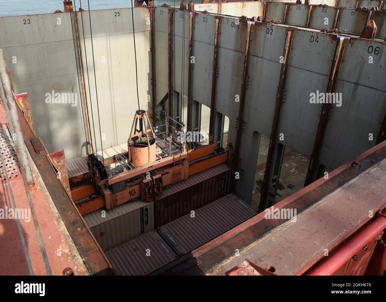A crane lowers shipping containers of munitions into the deep hold of ...